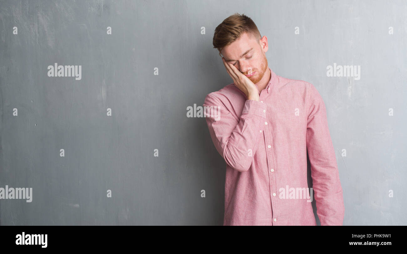 Young redhead man over grey grunge wall wearing pink shirt thinking ...