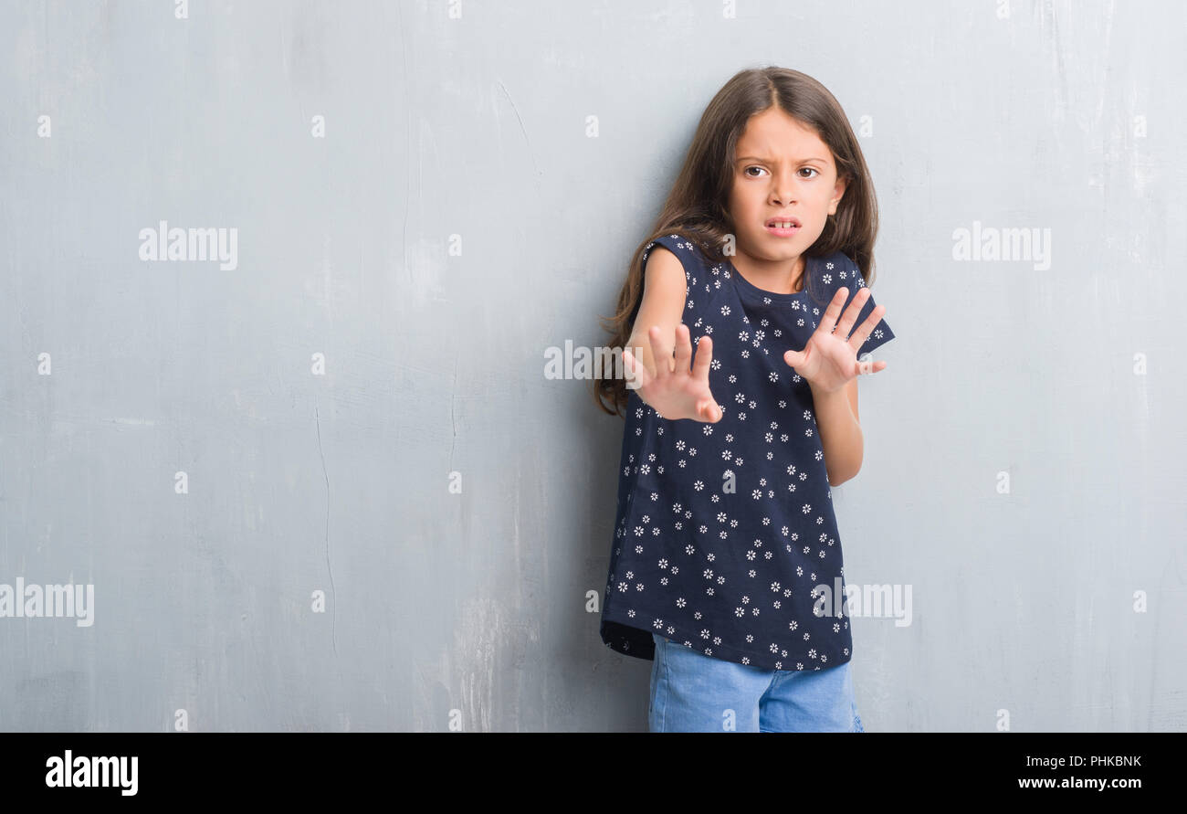 Young hispanic kid over grunge grey wall afraid and terrified with fear ...