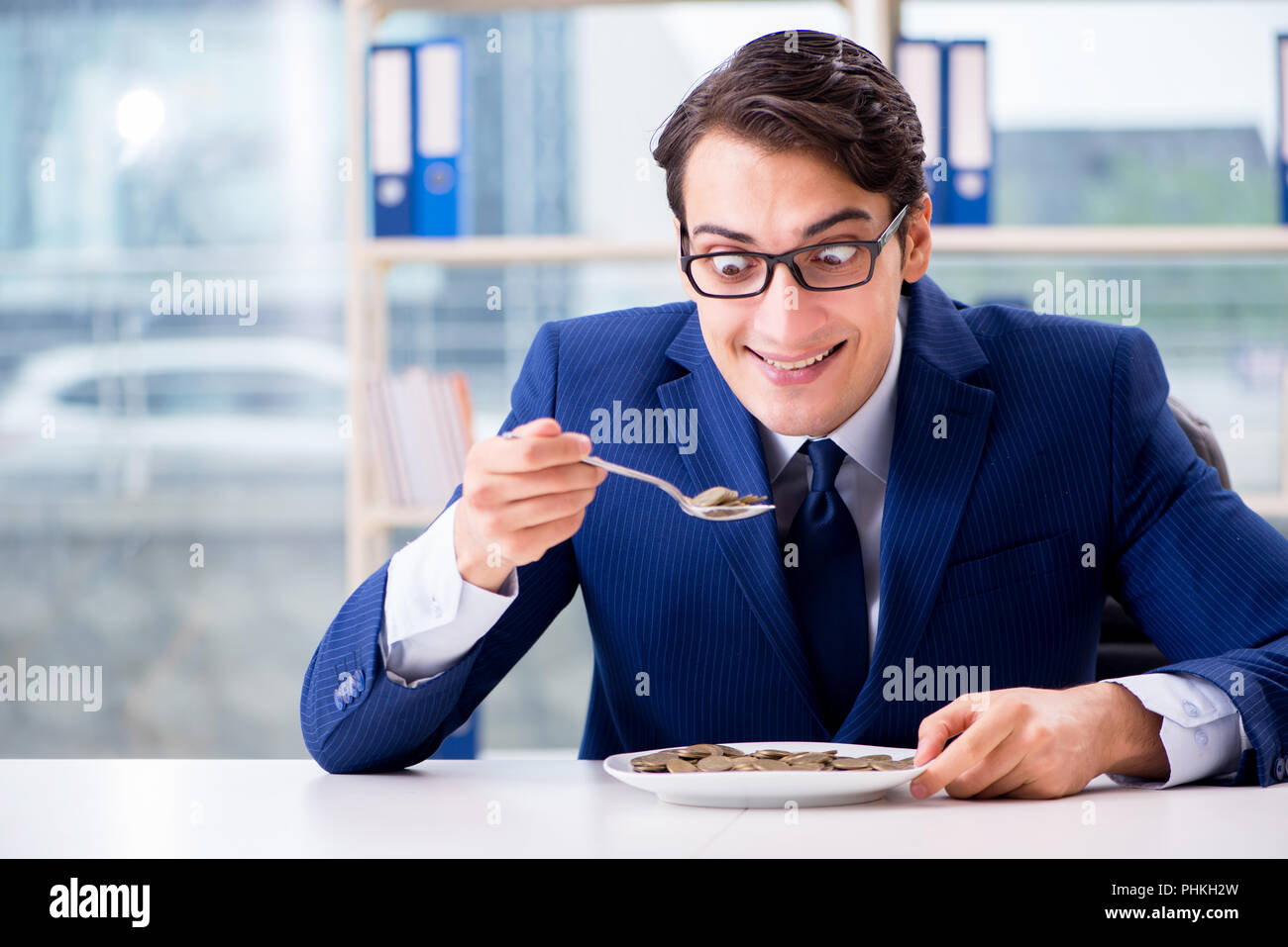 Funny businessman eating gold coins in office Stock Photo - Alamy