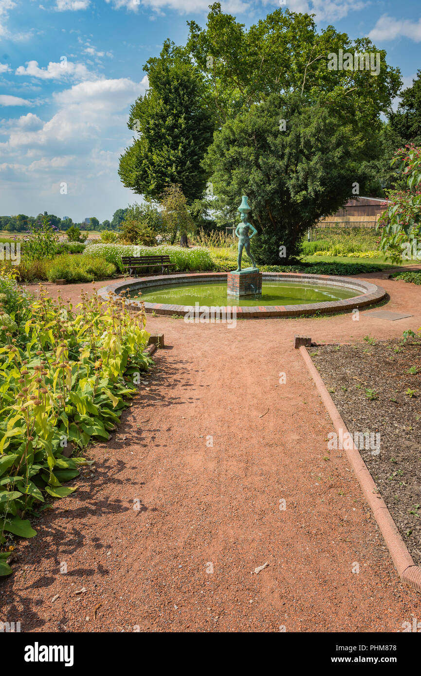 View of the statue, trees and flowers along a pathway at Rheinpark ...
