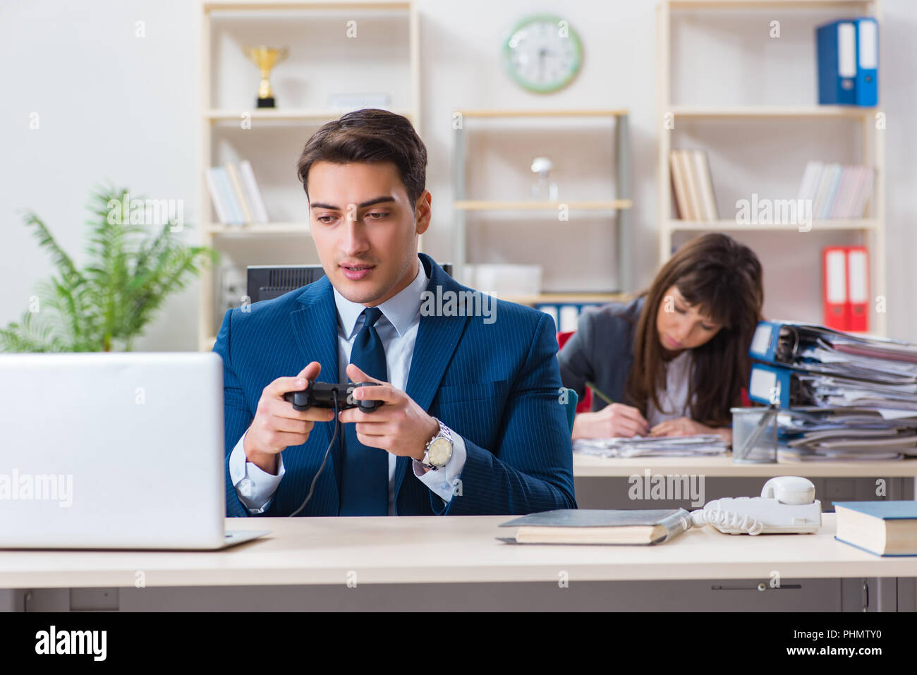 Man playing games in office while colleague is busy Stock Photo - Alamy