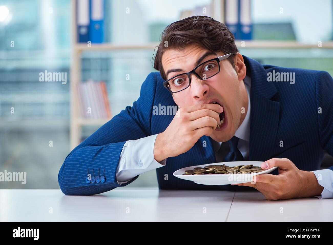 Funny businessman eating gold coins in office Stock Photo - Alamy