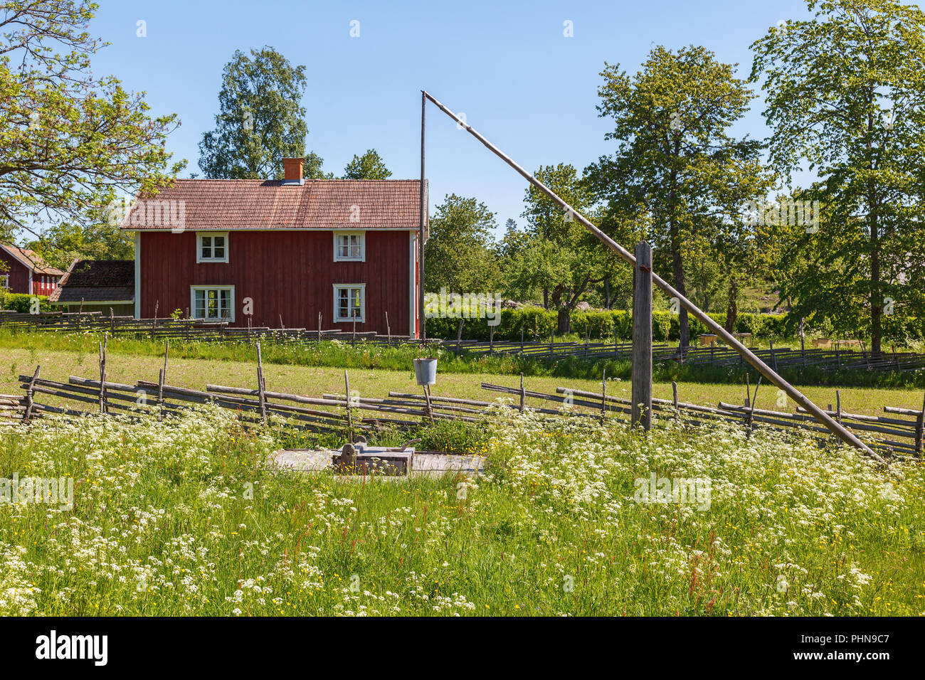 Water well in a meadow with a red cottage Stock Photo - Alamy