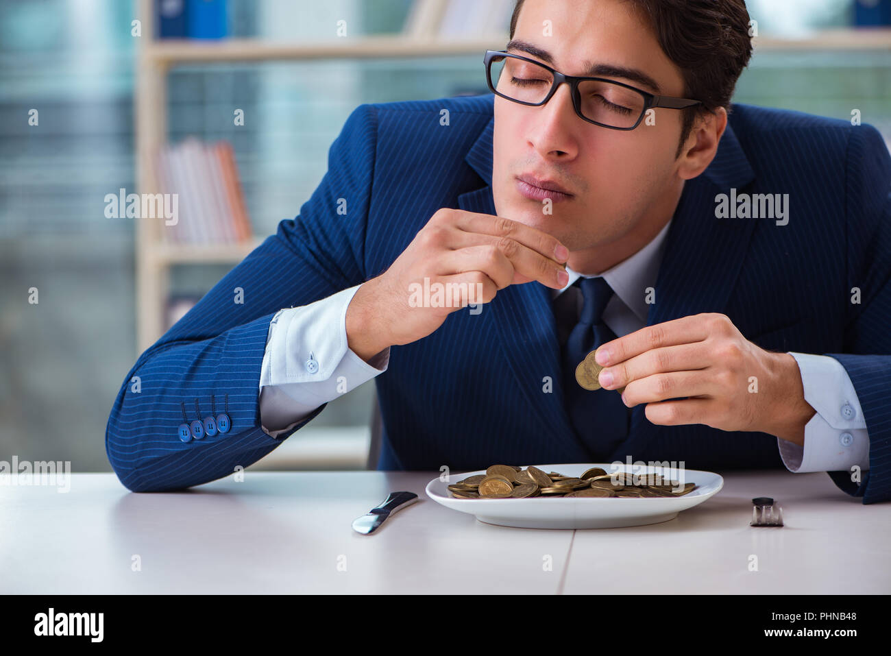 Funny businessman eating gold coins in office Stock Photo - Alamy