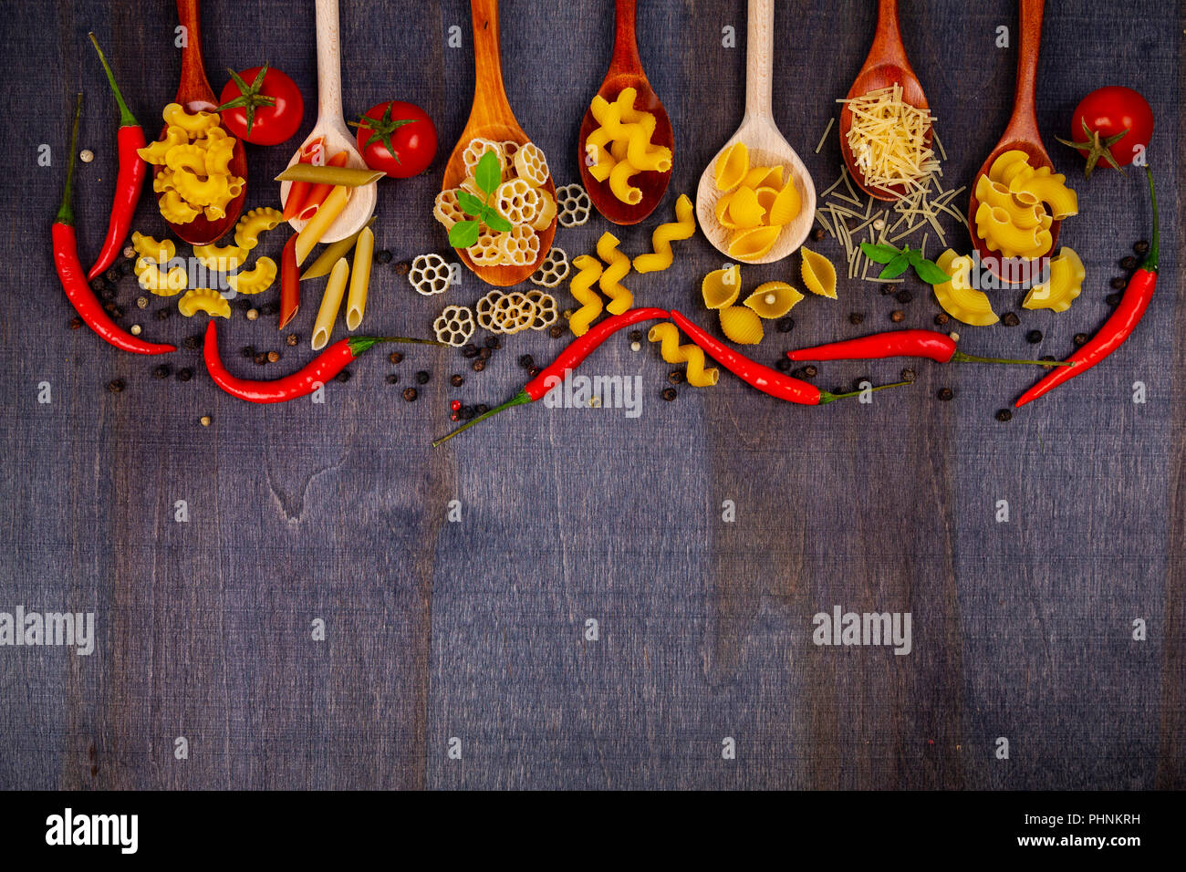 Different pasta in spoons on a dark wooden background, top view. Raw ...