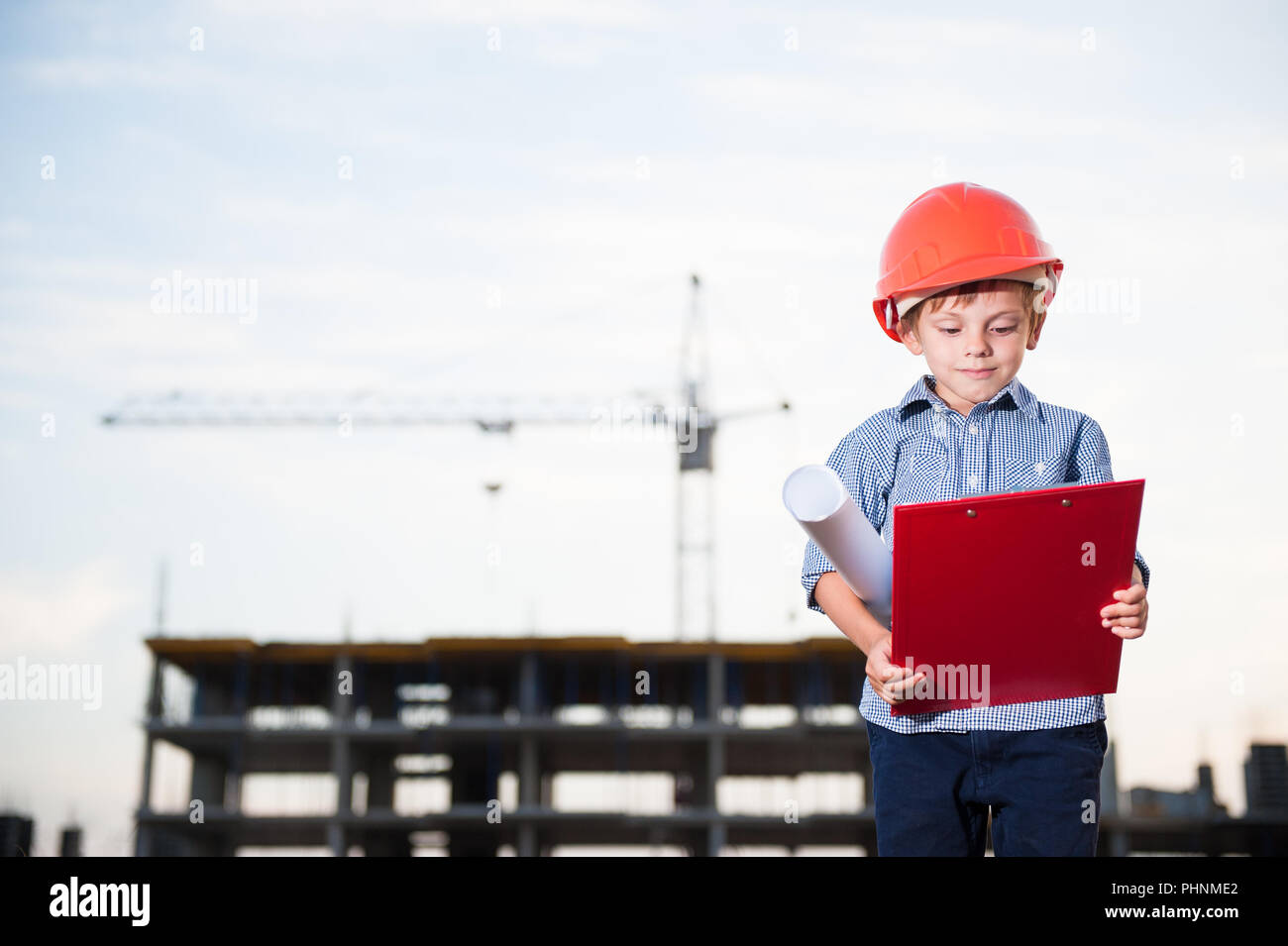 cute little boy in helmet with paper blueprint and folder in hands on ...