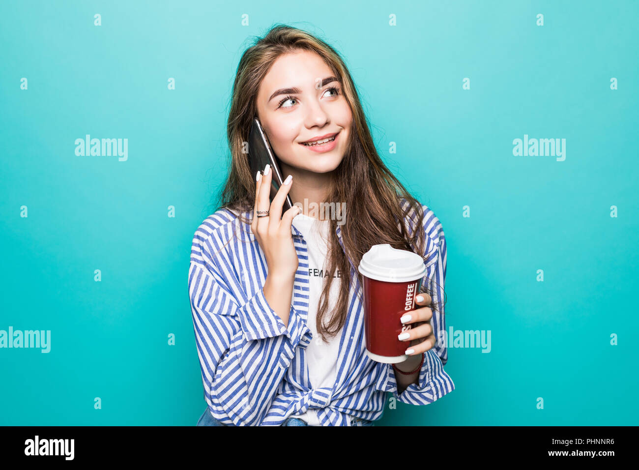 Portrait of a pretty woman using mobile phone while holding takeaway ...