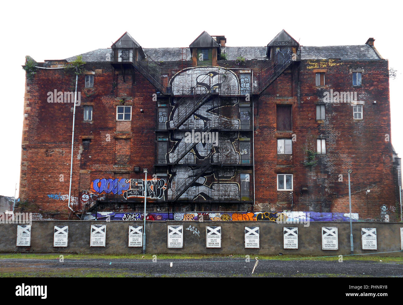 A huge derelict, empty and abandoned, red brick building sits on waste ...