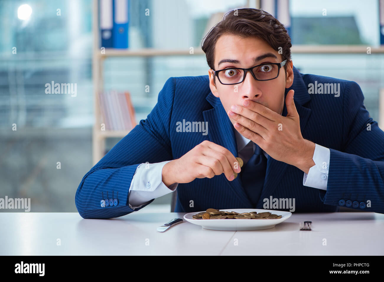 Funny businessman eating gold coins in office Stock Photo - Alamy