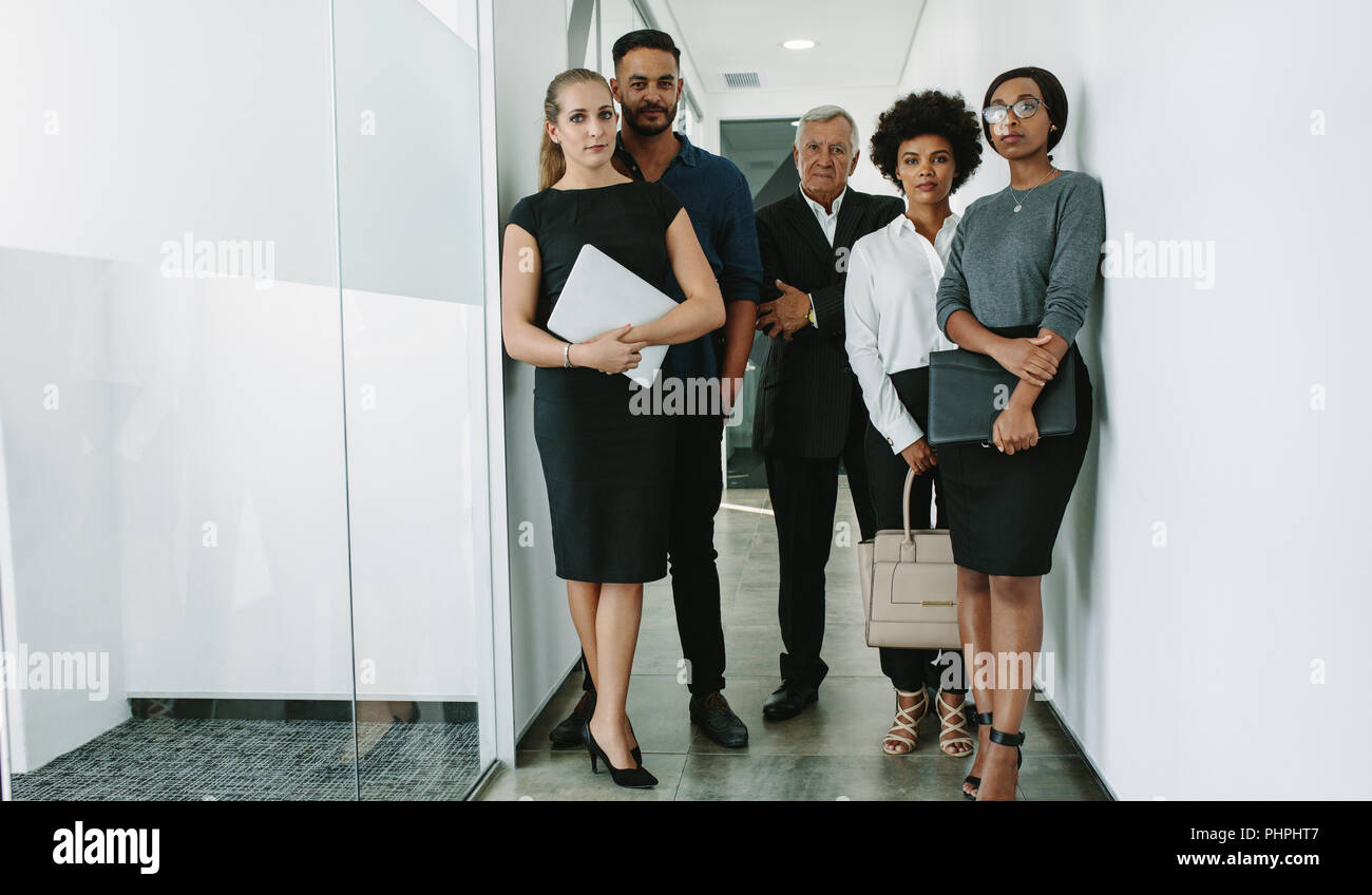 Portrait of diverse business professionals standing in office hallway ...