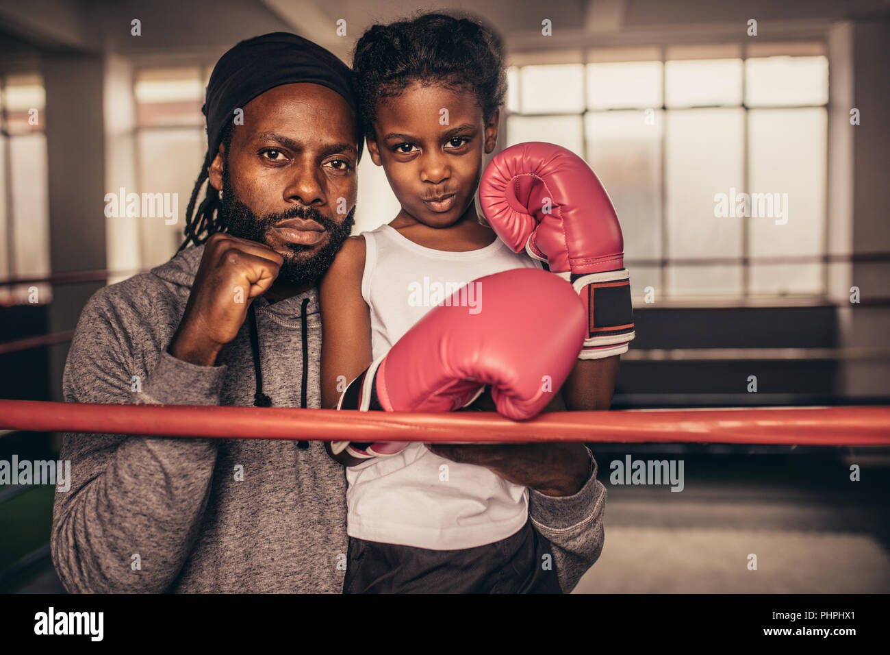 Kid wearing boxing gloves with her trainer standing in a boxing gym ...