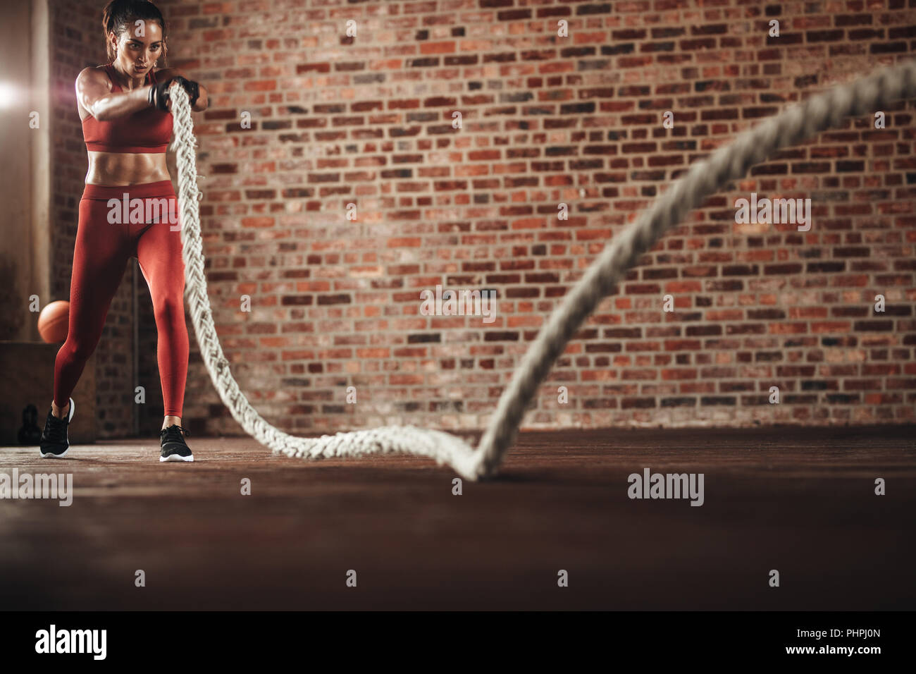 Fit female athlete moving a rope in wave motion as part of fat fitness ...