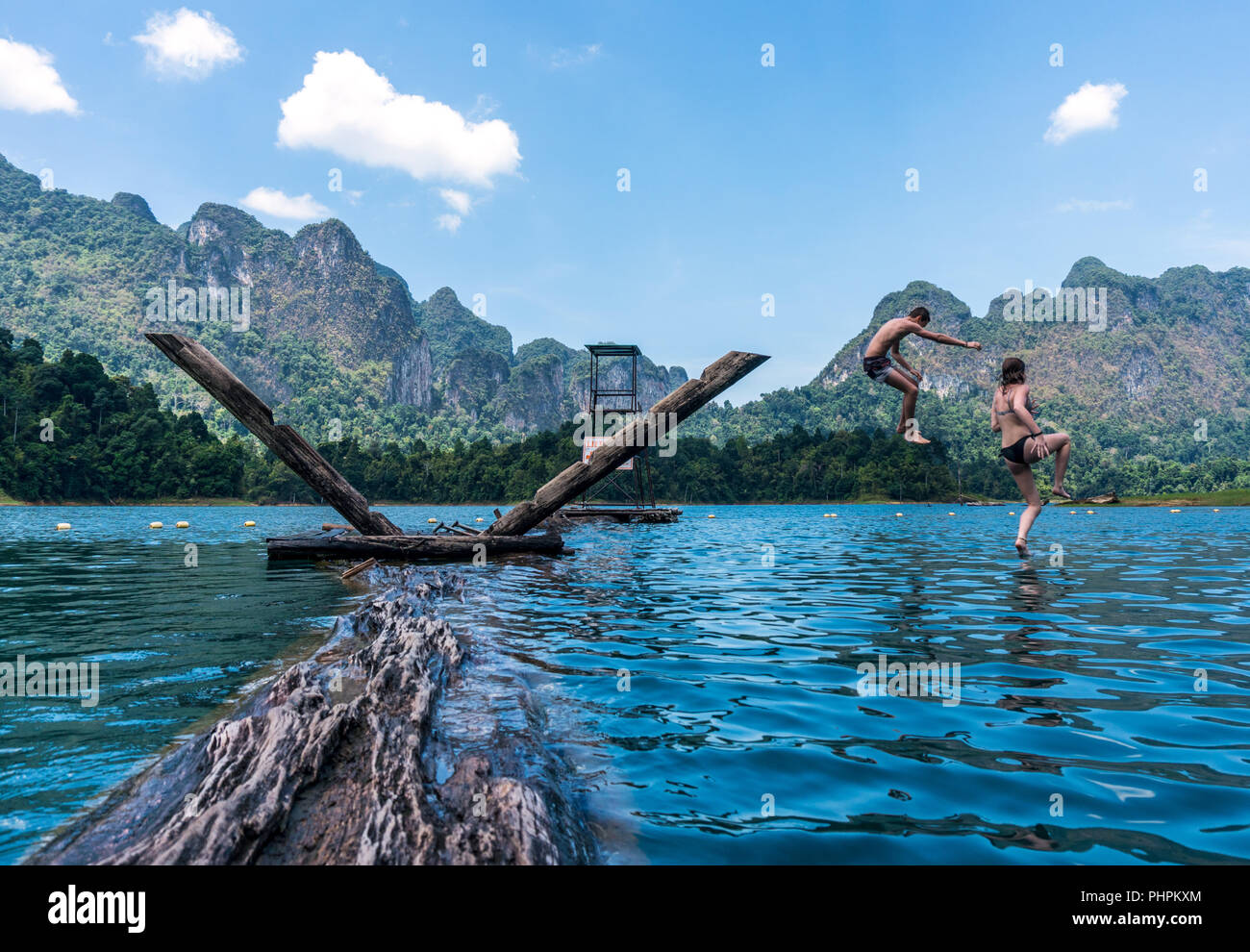 Two Teenage Kids Jumping in the lake with mountains and rain forest in ...