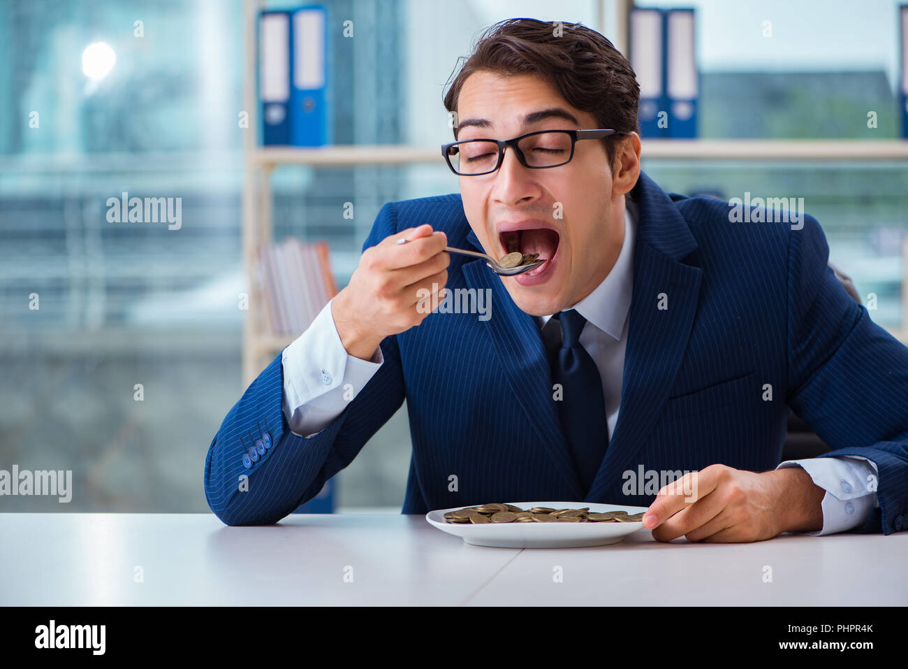 Funny businessman eating gold coins in office Stock Photo - Alamy
