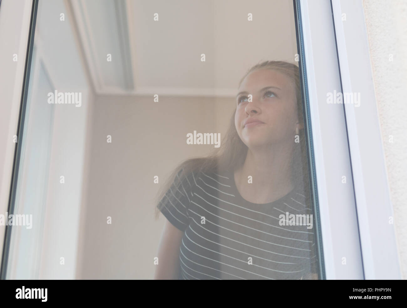 Young woman standing deep in thought staring out of a window in a low ...