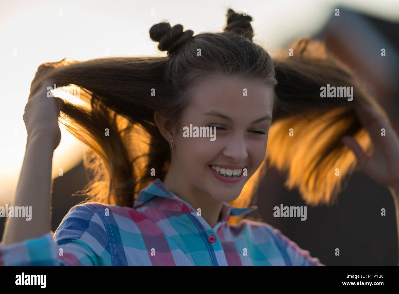 Happy playful young woman flicking her long hair with her hands backlit ...