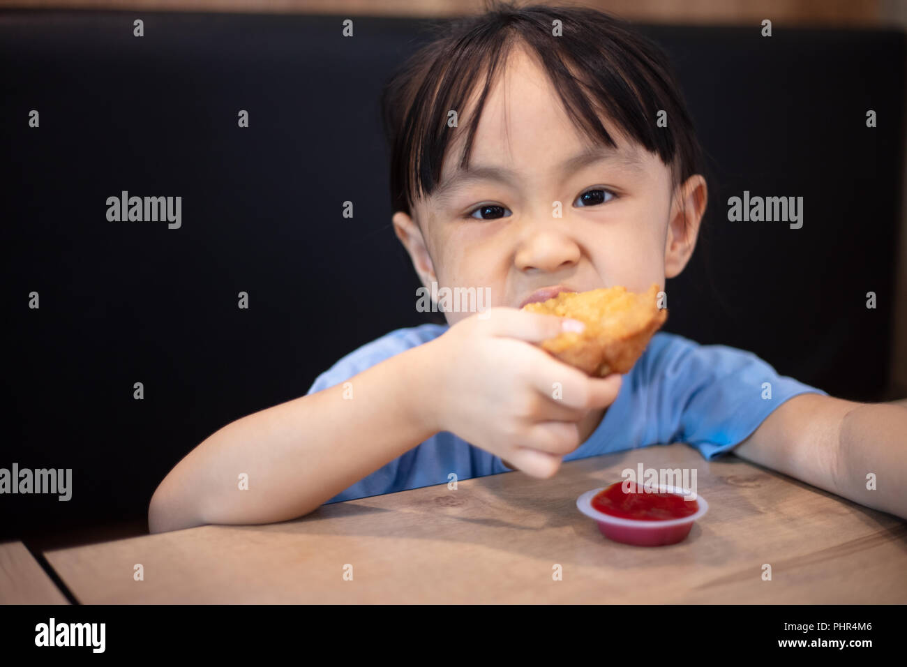 Asian Chinese little girl eating fried chicken at indoor restaurant ...