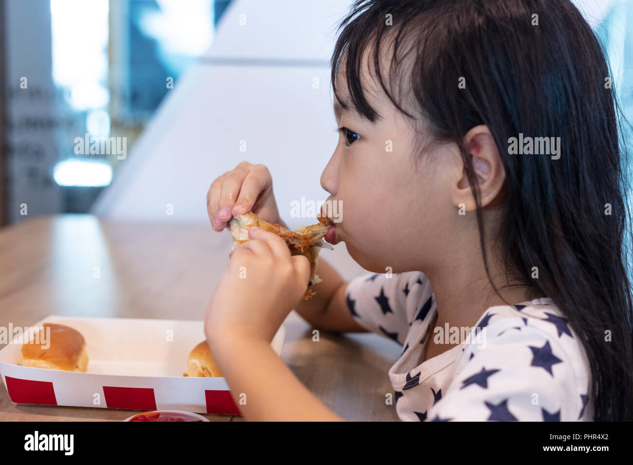 Asian Chinese little girl eating fried chicken at indoor restaurant ...