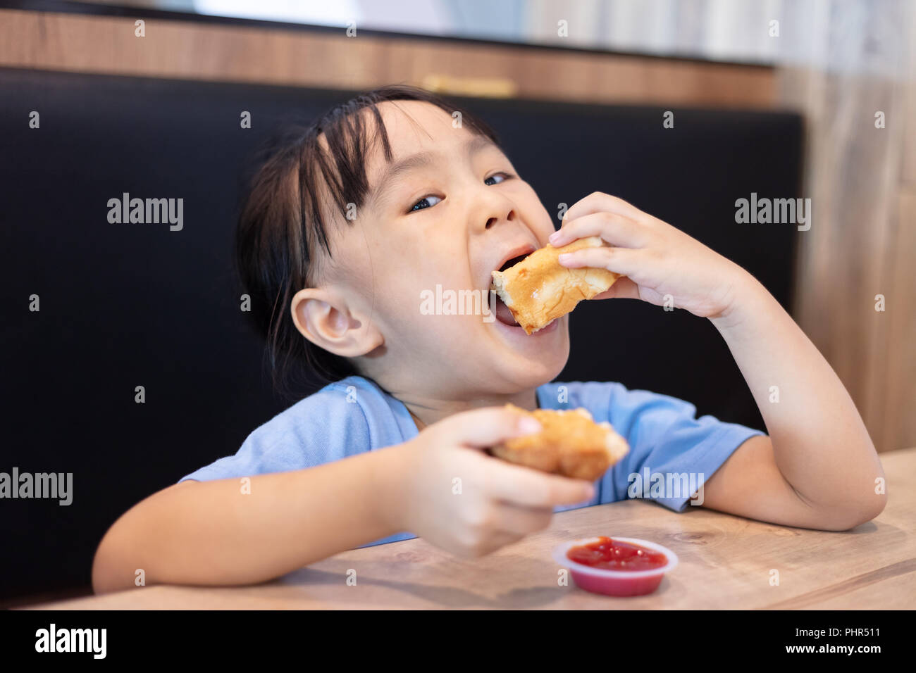 Asian Chinese little girl eating fried chicken at indoor restaurant ...
