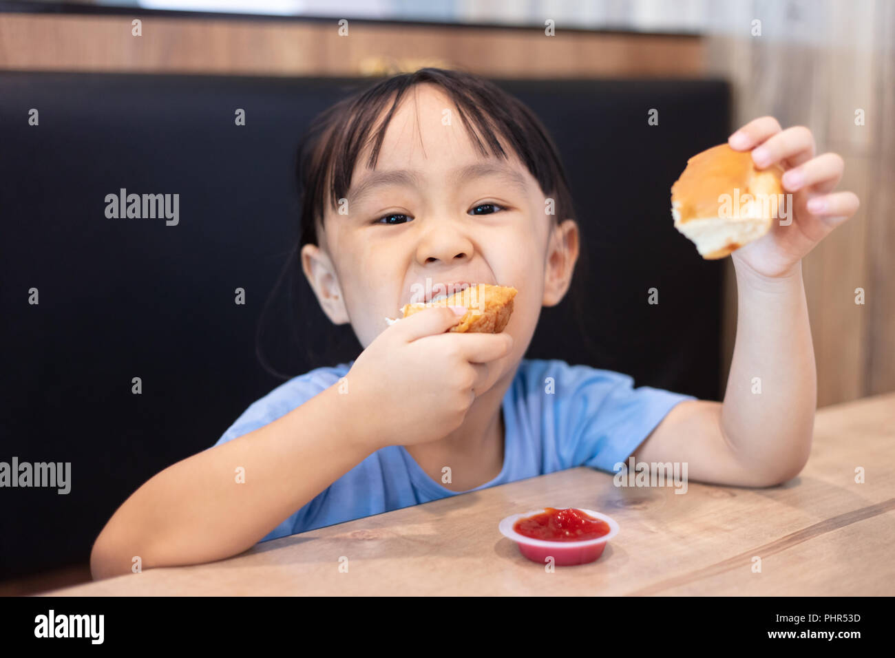 Asian Chinese little girl eating fried chicken at indoor restaurant ...