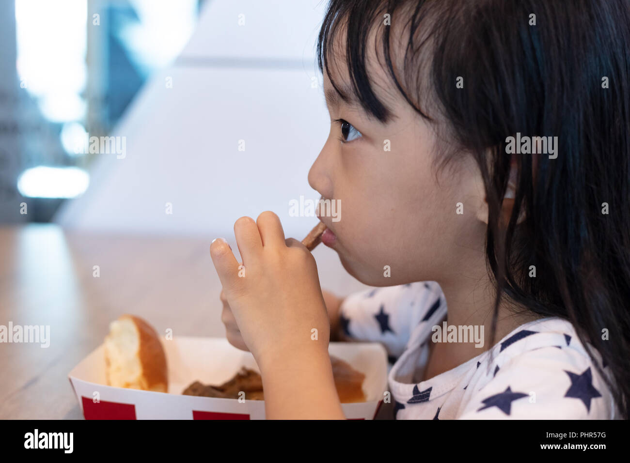 Asian Chinese little girl eating fried chicken at indoor restaurant ...