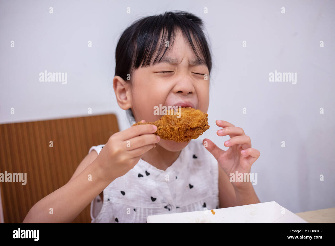 Asian Chinese little girl eating fried chicken at indoor restaurant ...