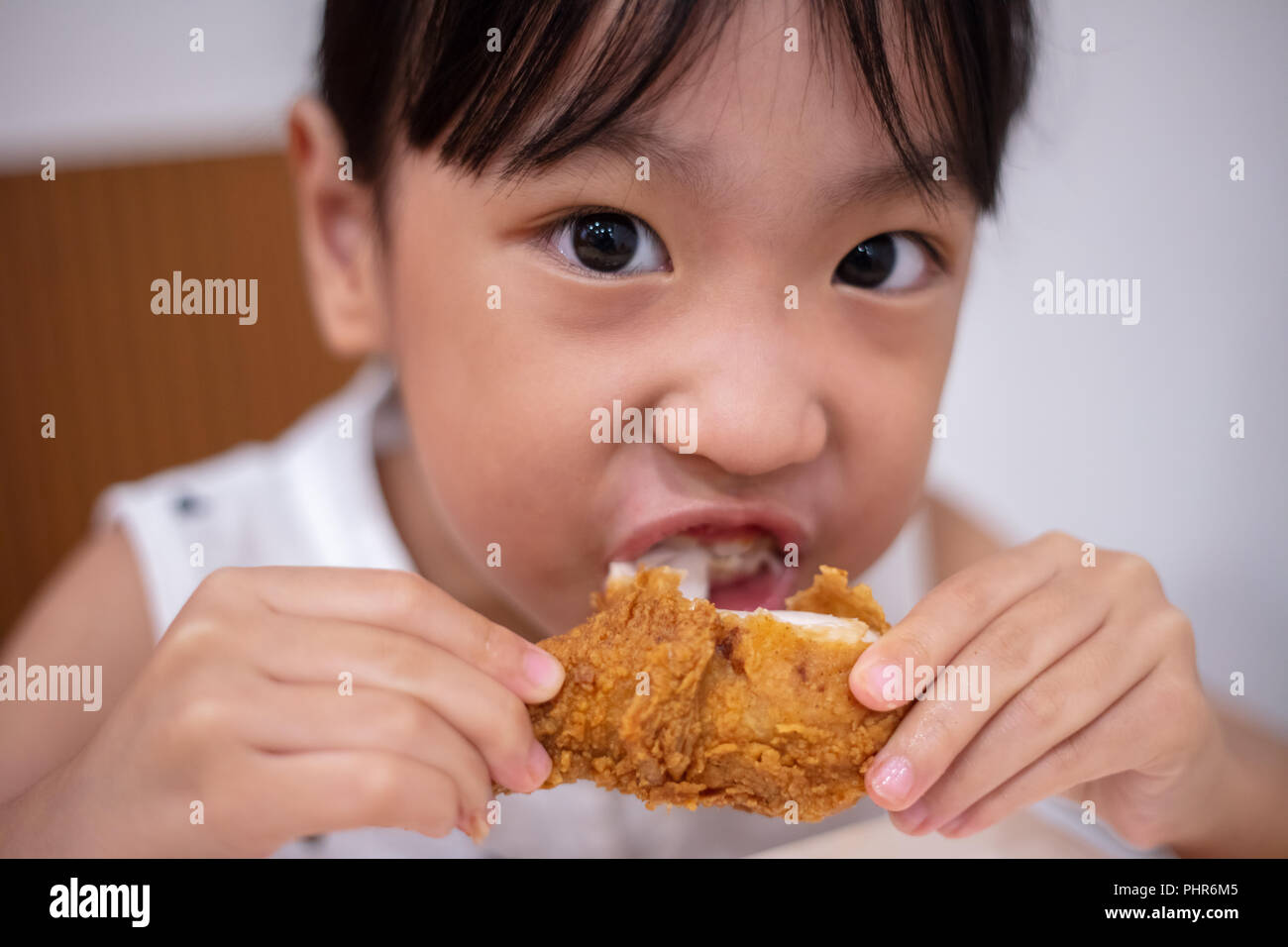 Asian Chinese little girl eating fried chicken at indoor restaurant ...