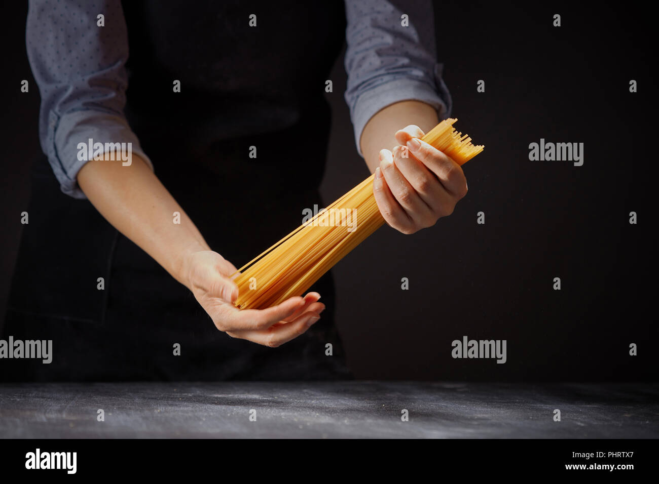 Woman's hand holding raw spaghetti on dark background Stock Photo - Alamy