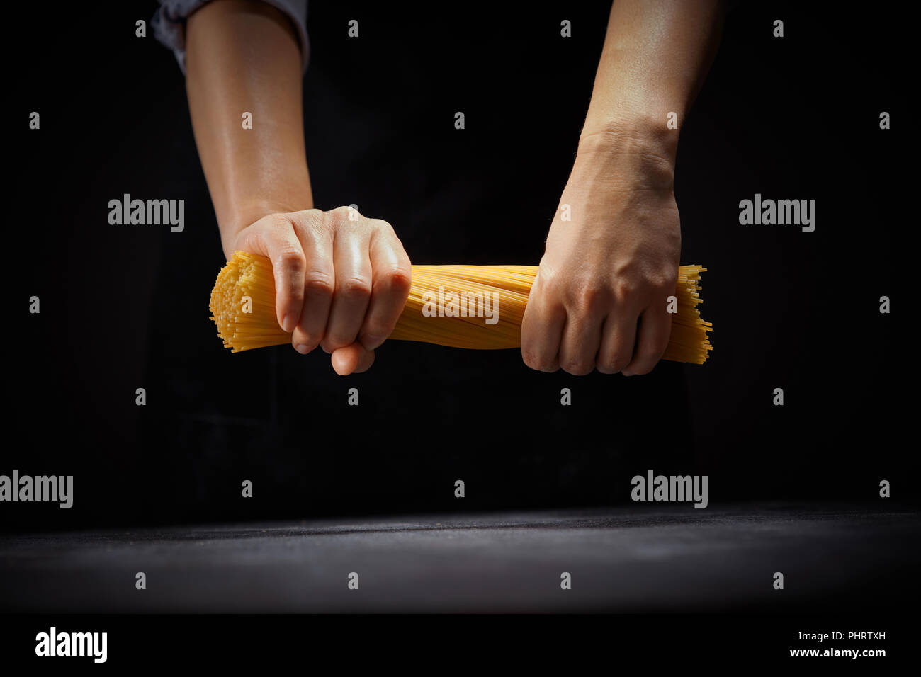 Chef breaking spaghetti with his hands on dark background Stock Photo ...