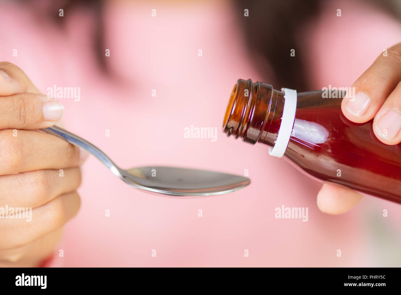 Woman hand pouring medication or antipyretic syrup from bottle to spoon ...
