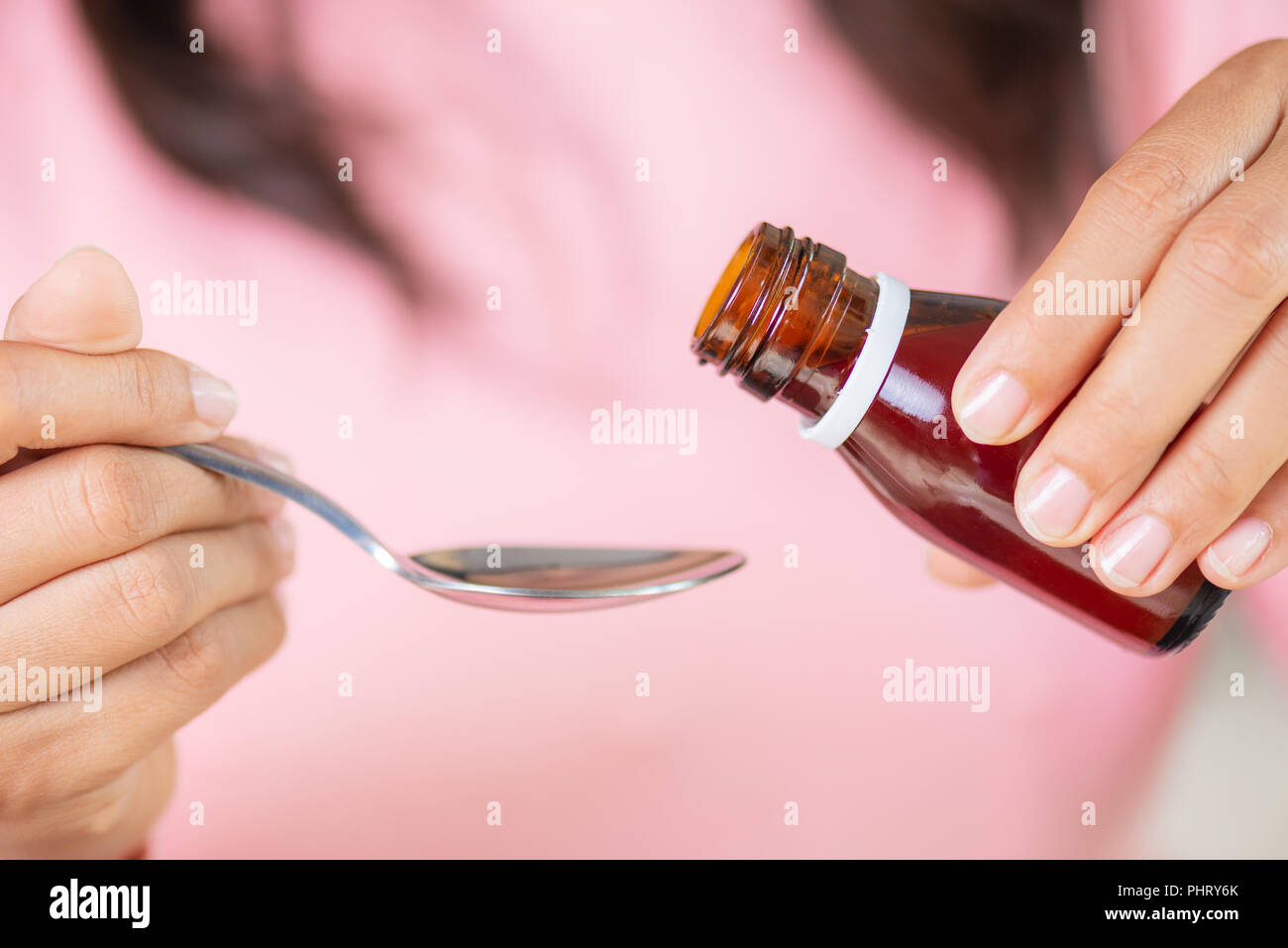 Woman hand pouring medication or antipyretic syrup from bottle to spoon ...