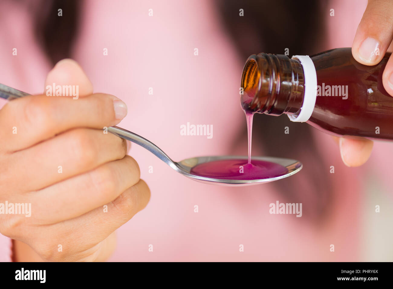 Woman hand pouring medication or antipyretic syrup from bottle to spoon ...