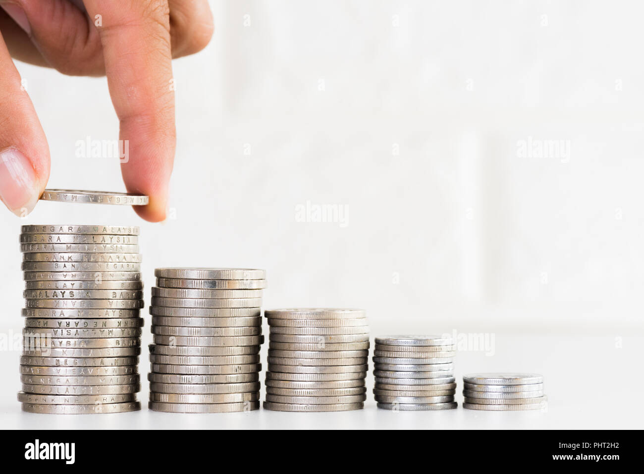 Woman hand put a coin on stacking coins on white brick block background ...