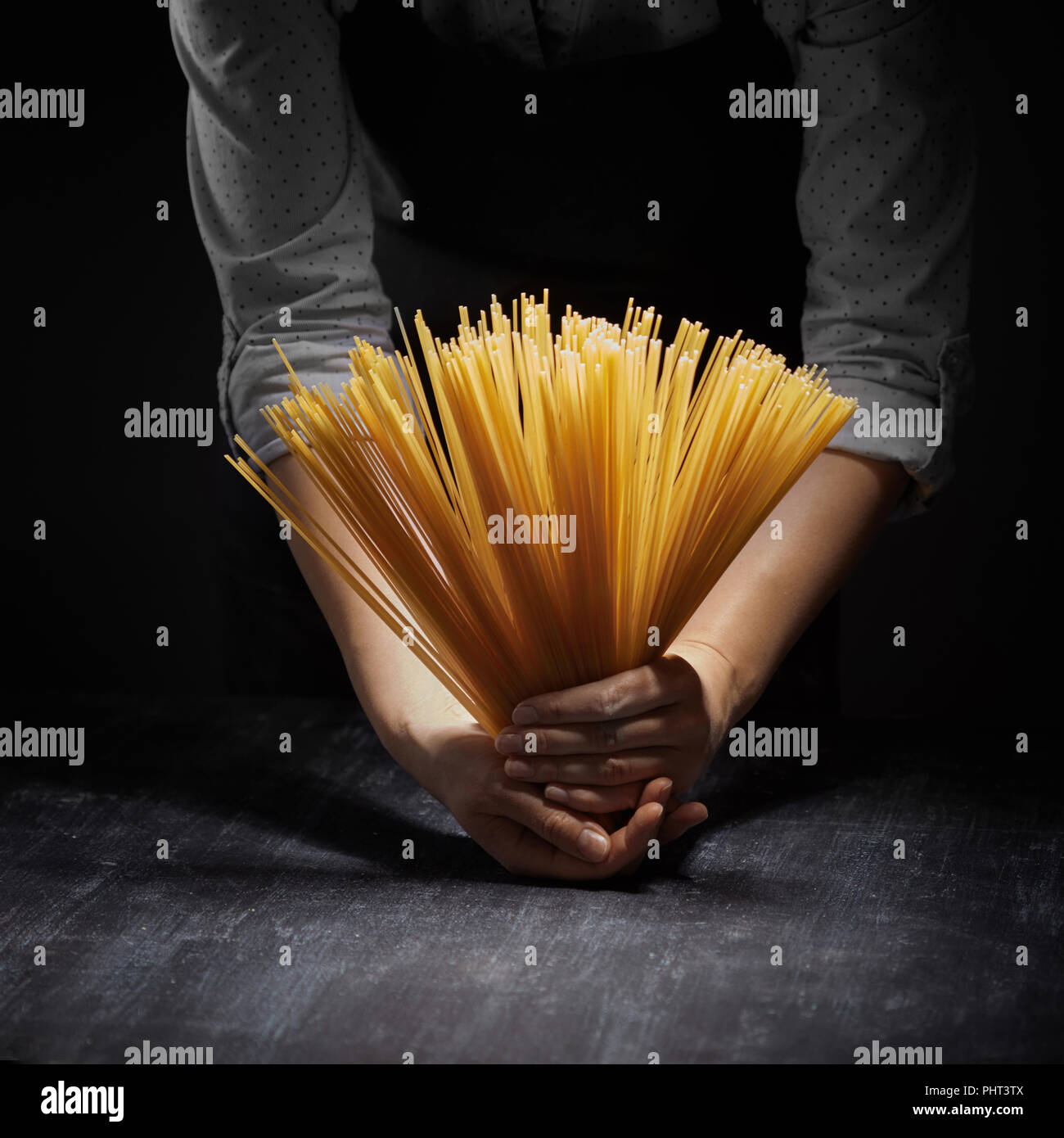 Woman's hands holding Raw spaghetti in dark background Stock Photo - Alamy
