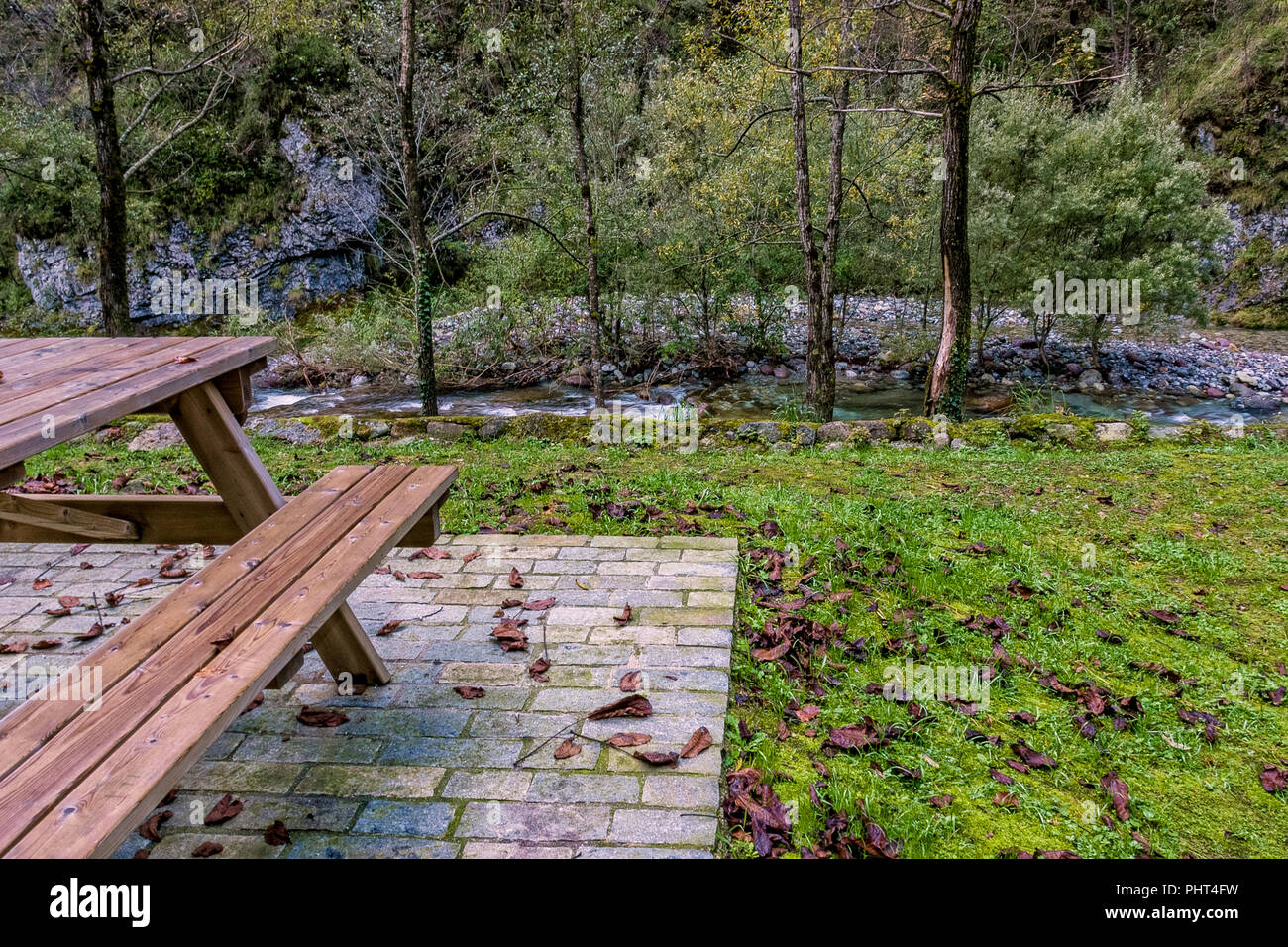 wooden picnic bench and table on the lawn along the mountain stream in ...