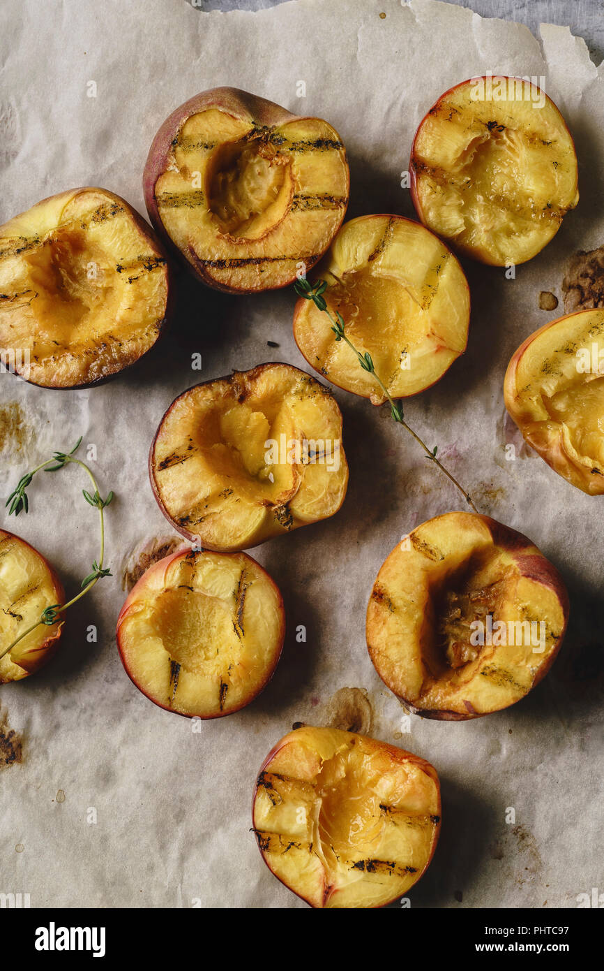 Grilled peaches and nectarines halved on baking paper sheet with thyme ...