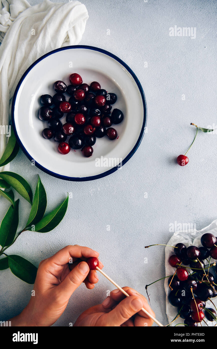 A woman pitting cherries using a wooden skewer on a grey background ...