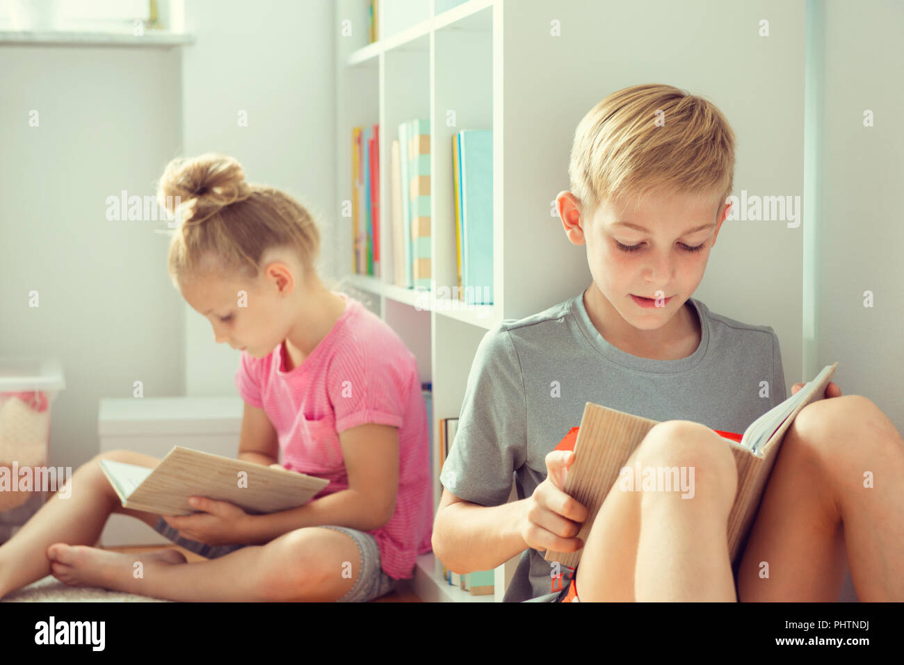 Two happy children reading books on the floor at the school library ...