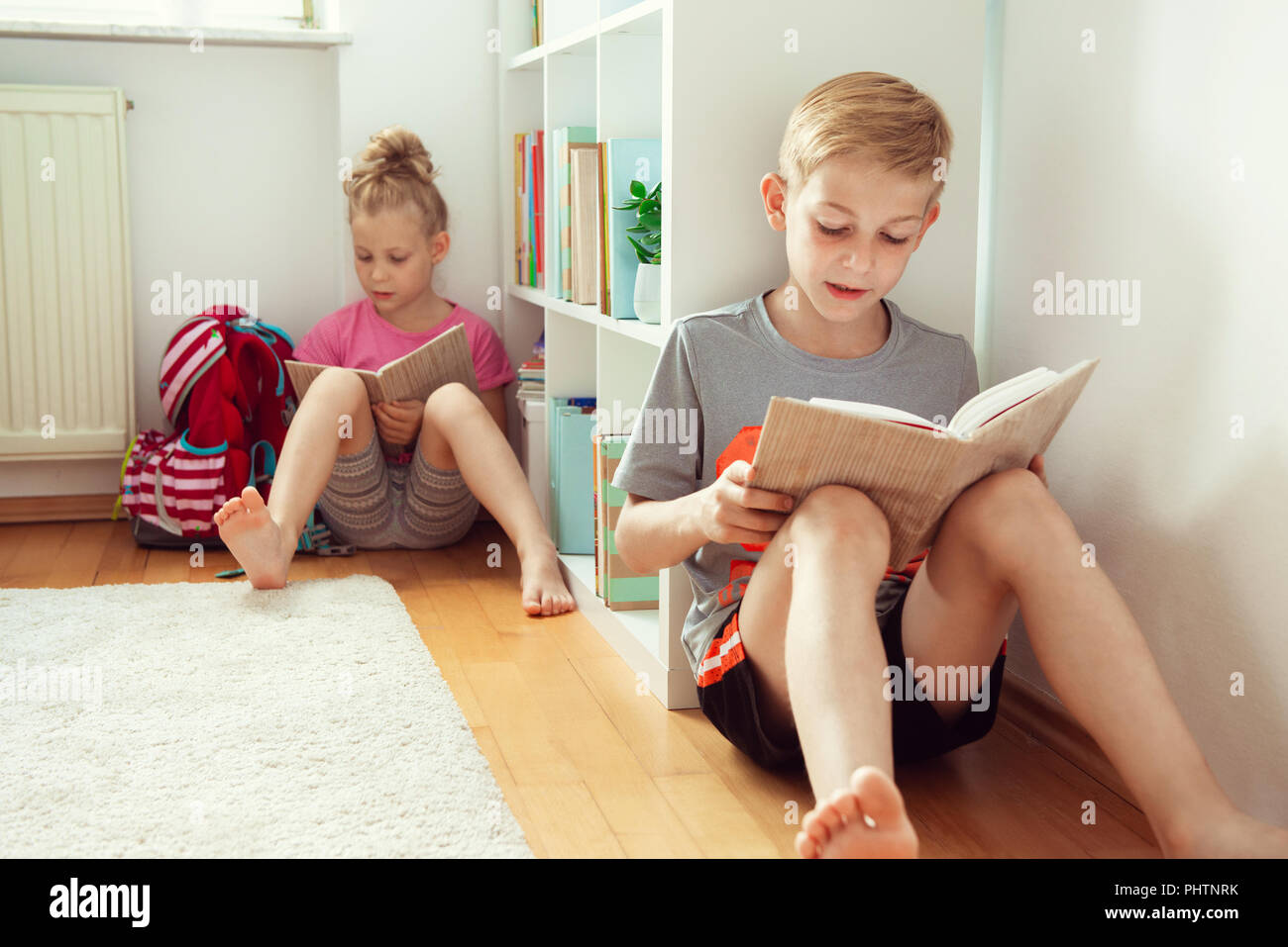 Two happy children reading books on the floor at the school library ...