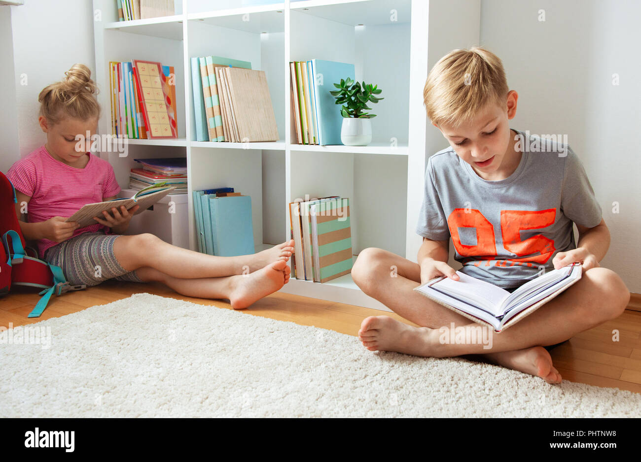 Two happy children reading books on the floor at the school library ...