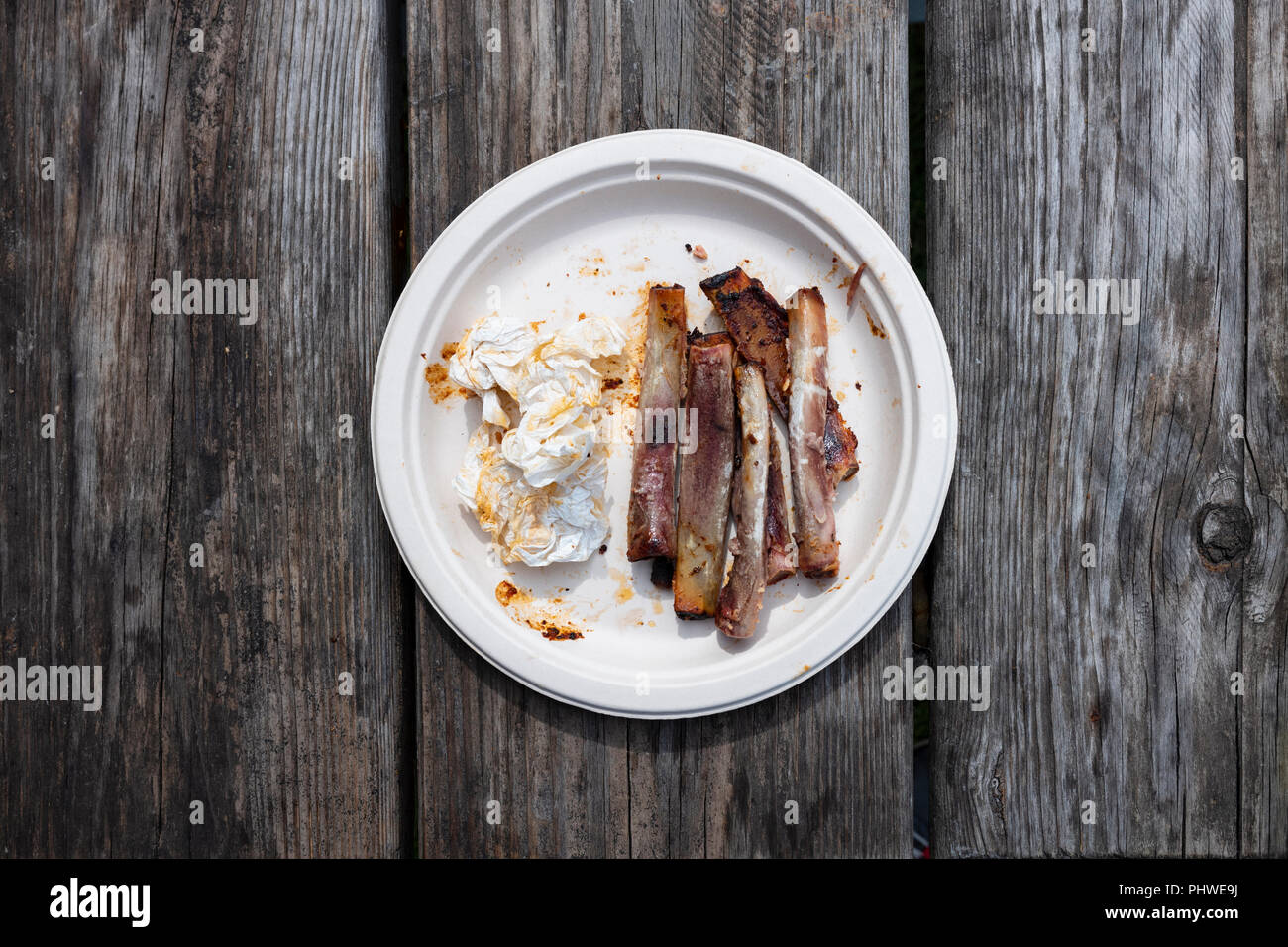 A paper plate full of eaten barbecue ribs on a wooden picnic table at ...