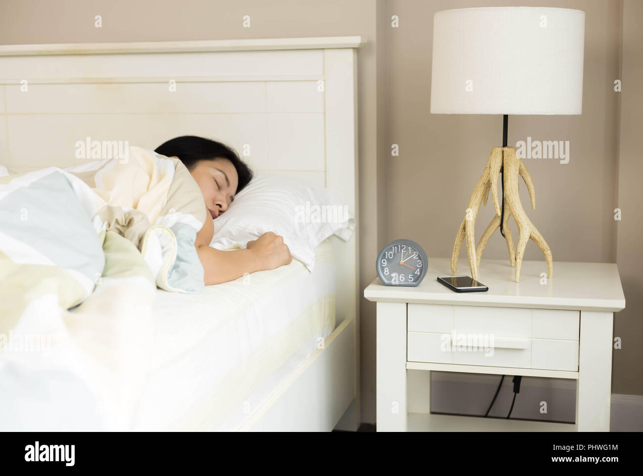 Alarm clock standing on bedside table with woman in bed sleeping in ...