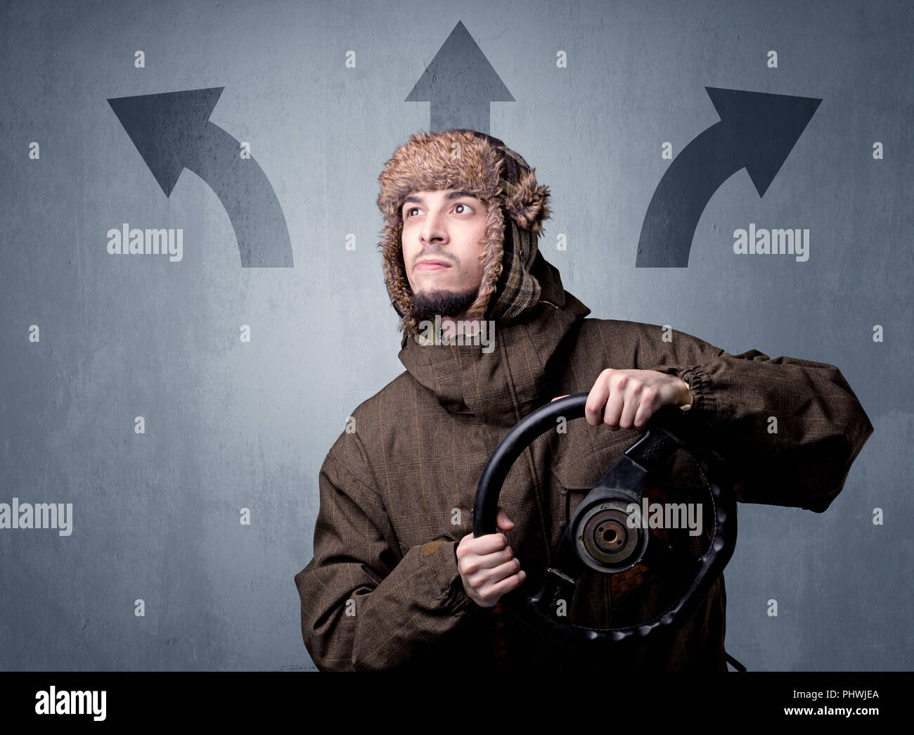 Young man holding black steering wheel with three arrows above his head ...
