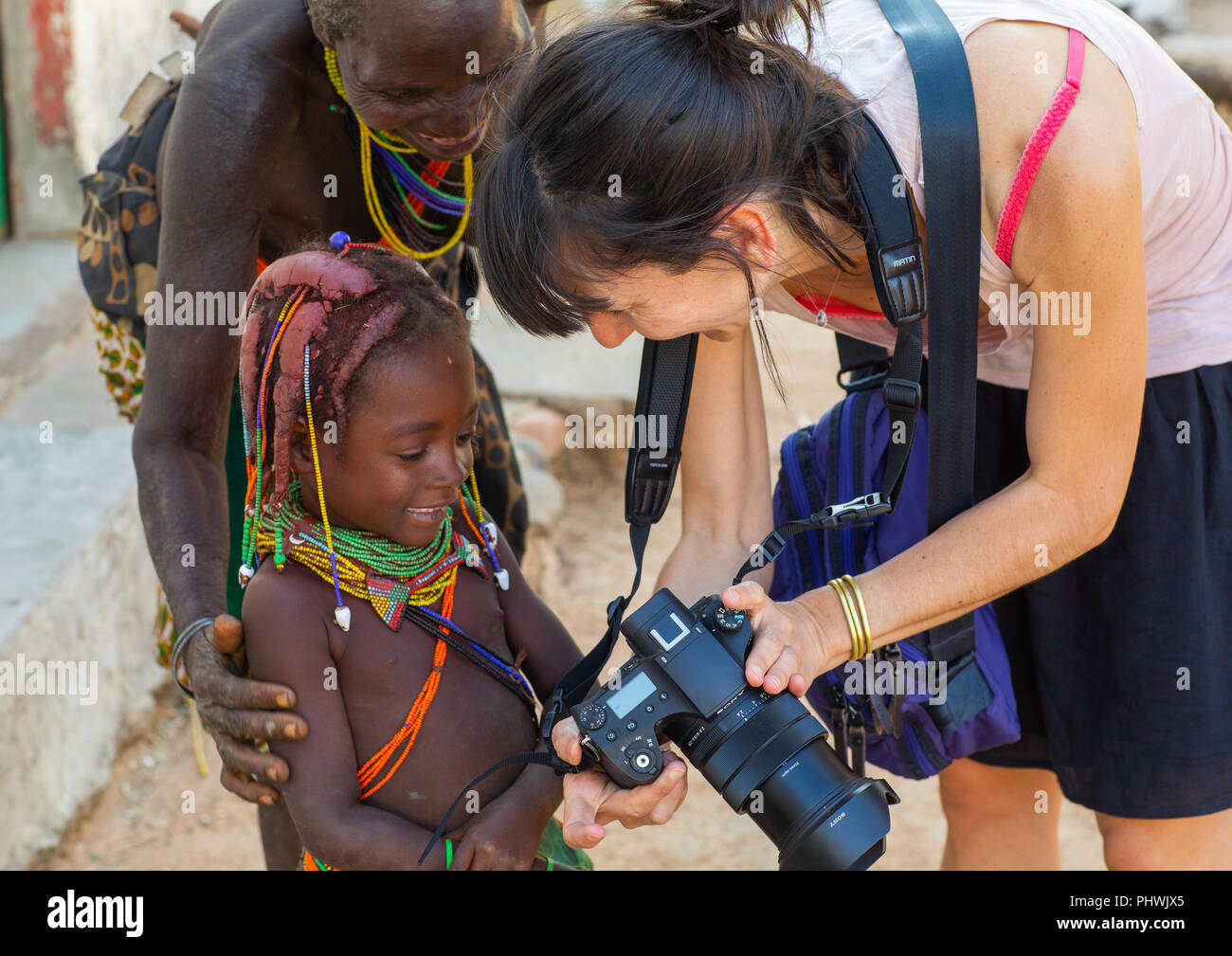 European tourist showing her camera screen to a mumuhuila tribe girl ...