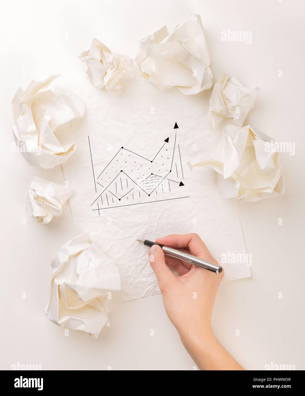 Female hand next to a few crumpled paper balls drawing a progress chart ...