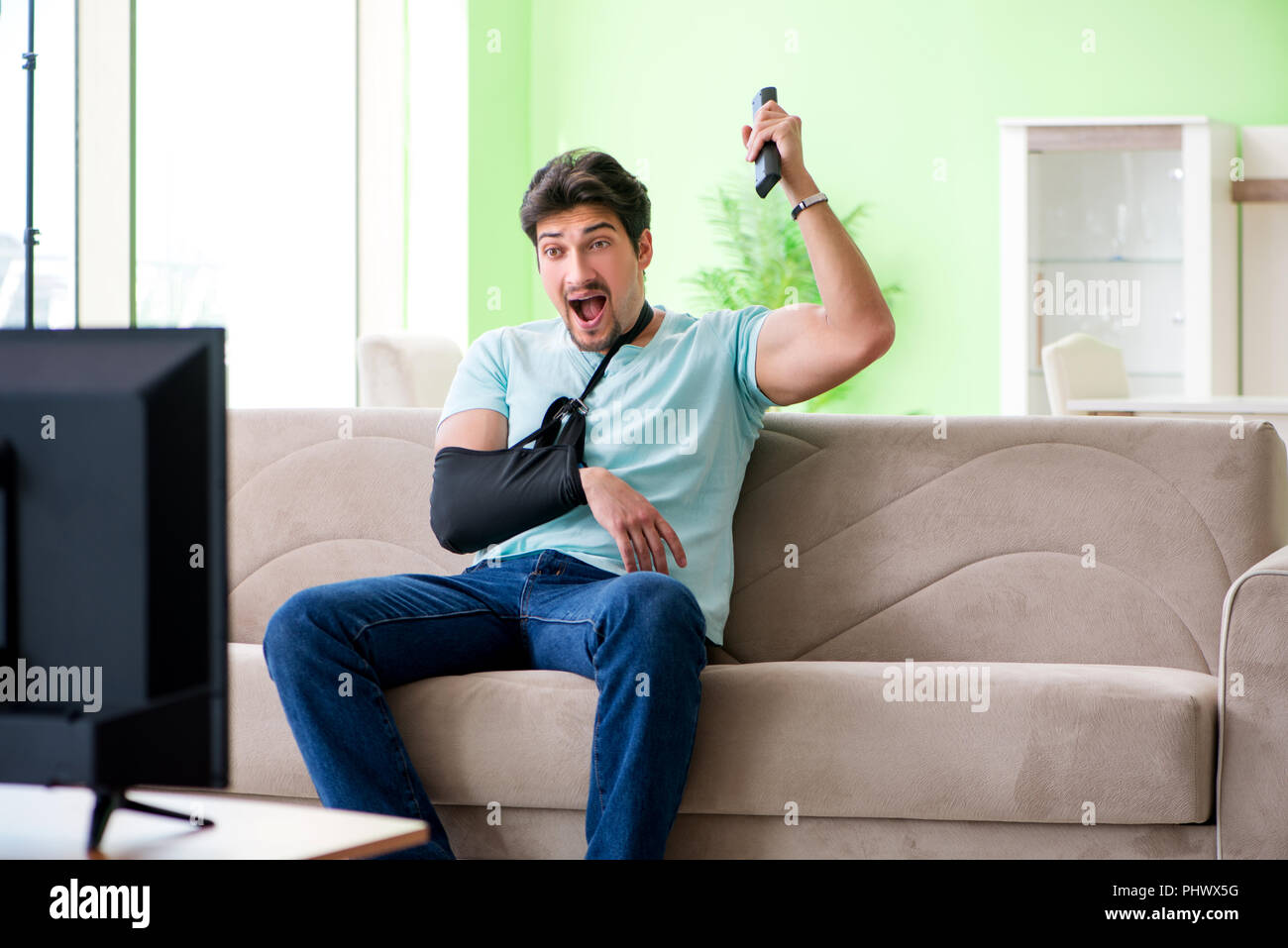 Arm injured man sitting on the sofa watching tv Stock Photo - Alamy