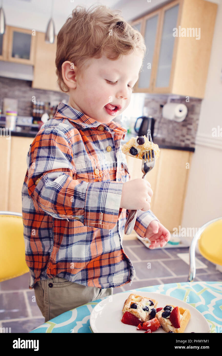Portrait of one happy kid boy eating breakfast waffles with fruits with ...