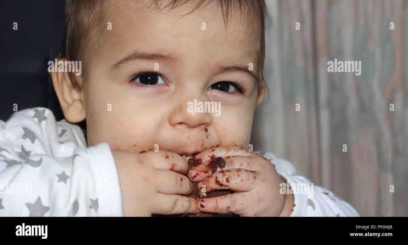 Baby boy eating a cookie in highchair Stock Photo - Alamy