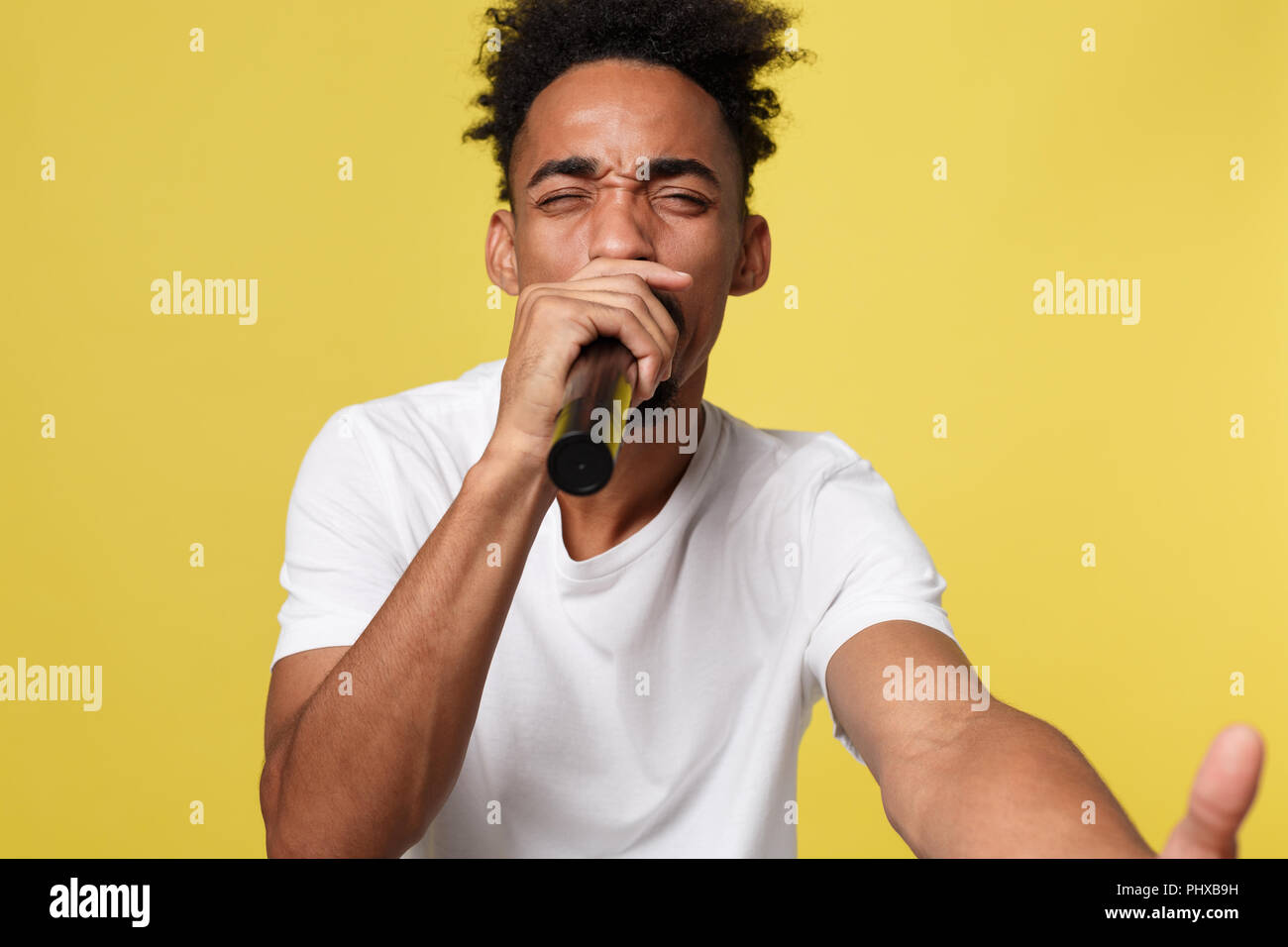 Stylish afro american man singing into microphone isolated on a yellow ...