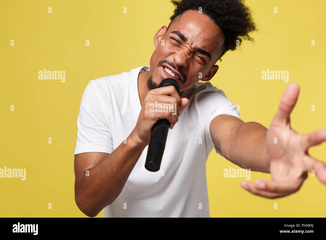 Stylish afro american man singing into microphone isolated on a yellow ...